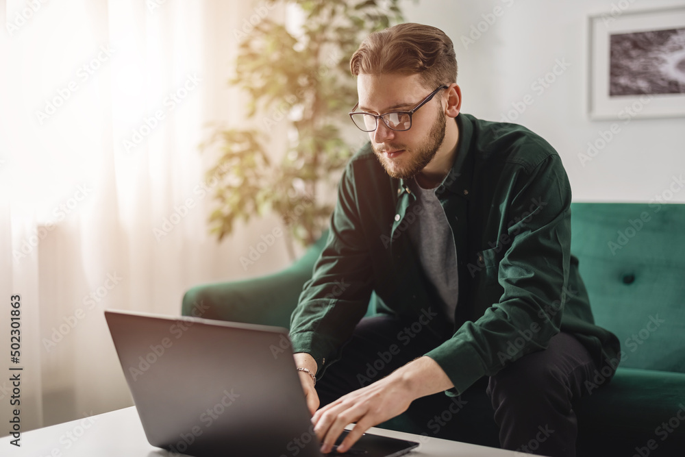 Young busy man in eyeglasses sitting on cozy sofa and working ...