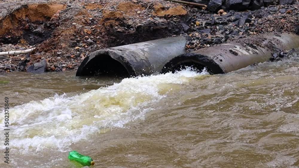 A strong stream of water flows out of a reinforced concrete culvert ...