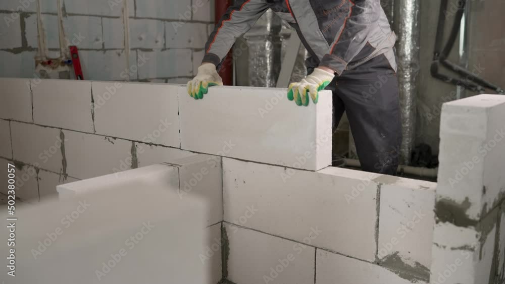 Construction site of a house made of light bricks. The master builds a ...