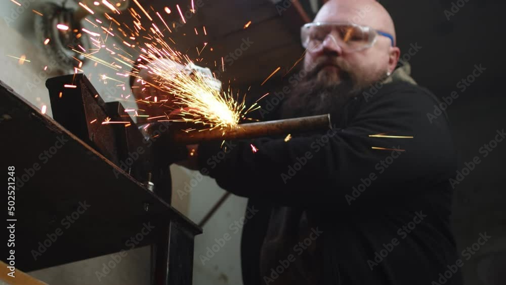 Man in protective glasses processes metal pipe with sandpaper attached ...