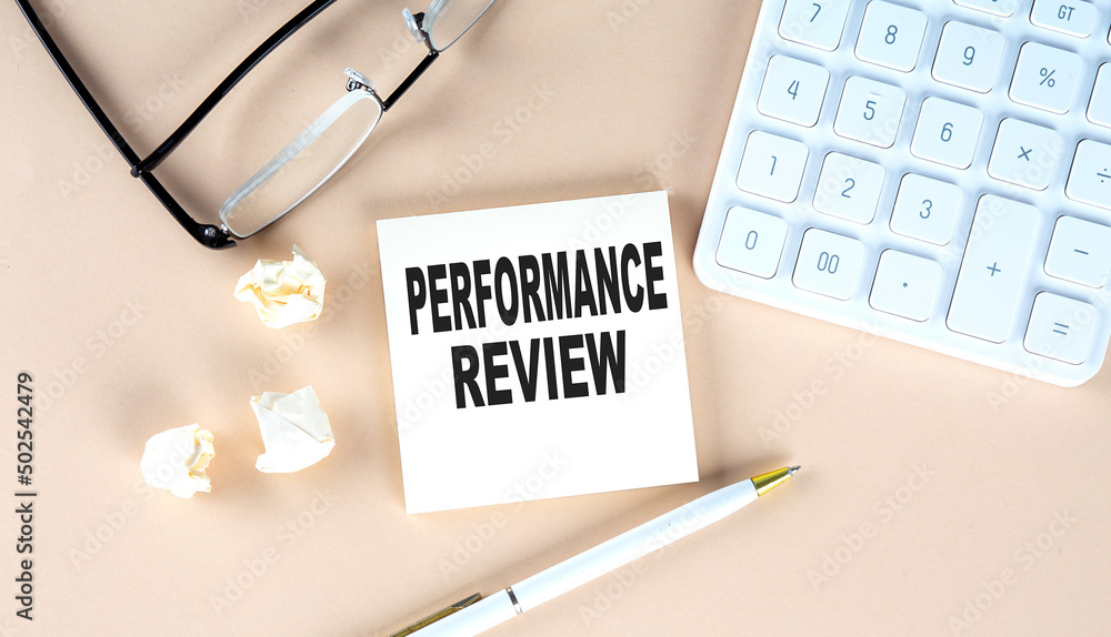 PERFORMANCE REVIEW text on sticky with pen ,calculator and glasses on a ...