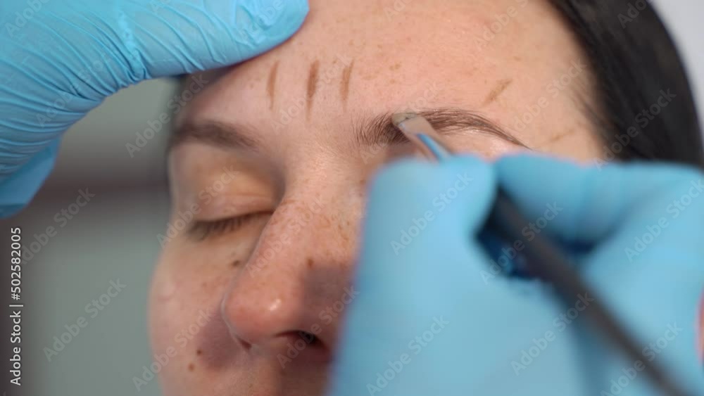 a young woman close-up paints her eyebrows with henna. markings are ...