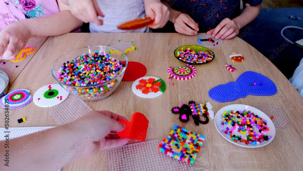 close-up of children's hands creating perler bead patterns, make crafts ...
