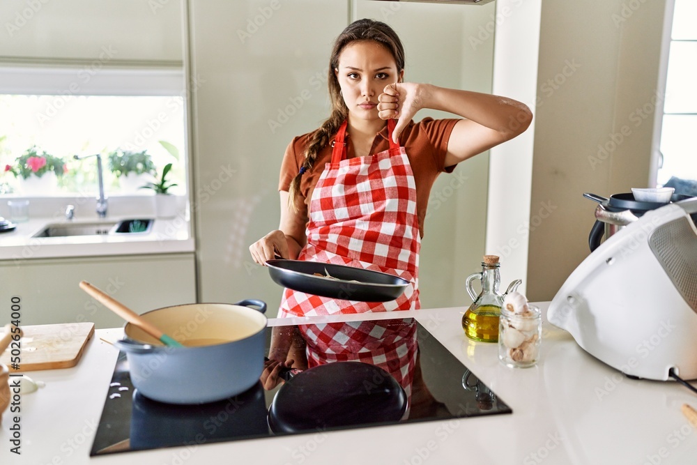 Beautiful young brunette woman wearing apron cooking at the kitchen ...