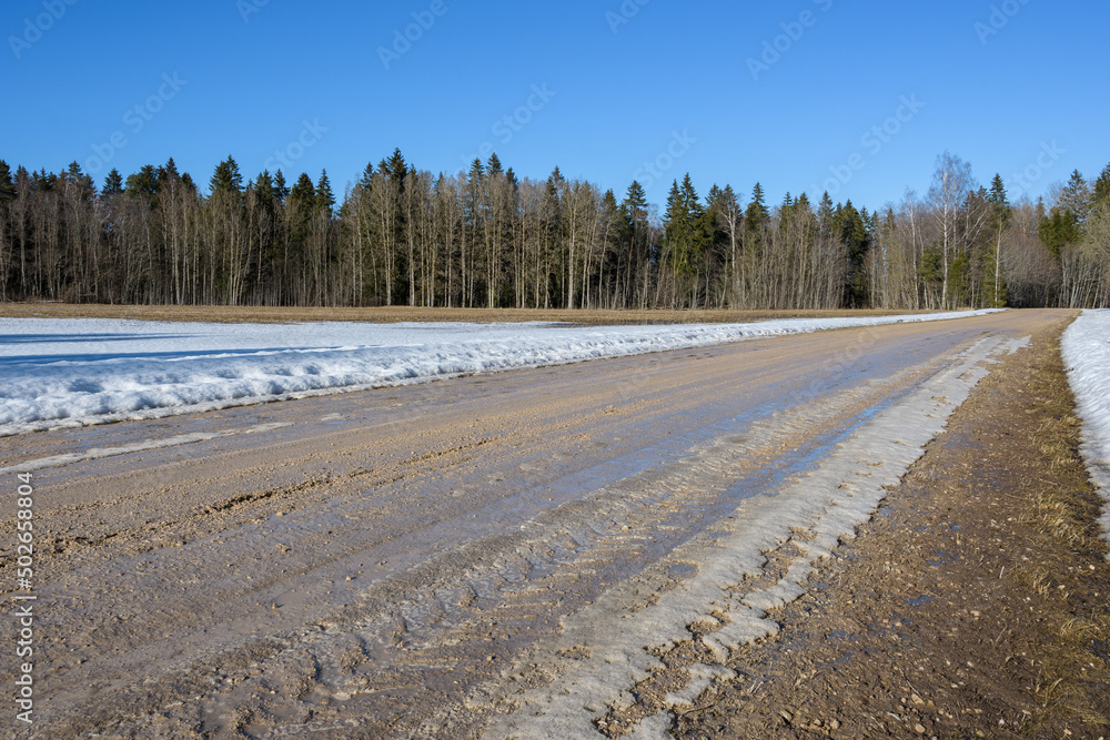 Foto de Straight dirt road with mud and melting ice crust among snow ...
