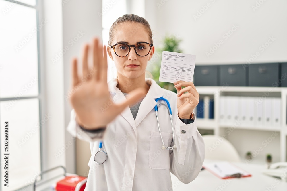 Young doctor woman holding covid certificate with open hand doing stop ...