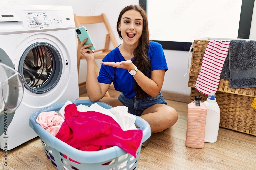 Young brunette woman doing laundry using smartphone pointing aside with ...