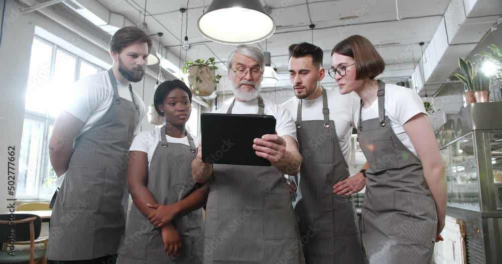 Caucasian old senior chef cook with tablet device in hands giving ...