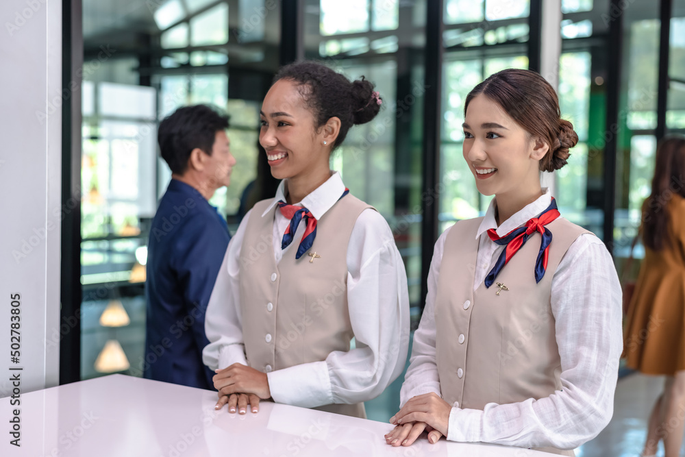 Two friendly Airport workers in uniforms smiling at check in counter ...