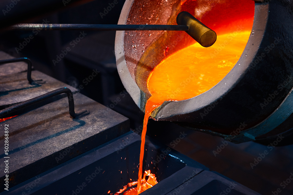 Pouring molten metal from a ladle into a rectangular graphite mold ...
