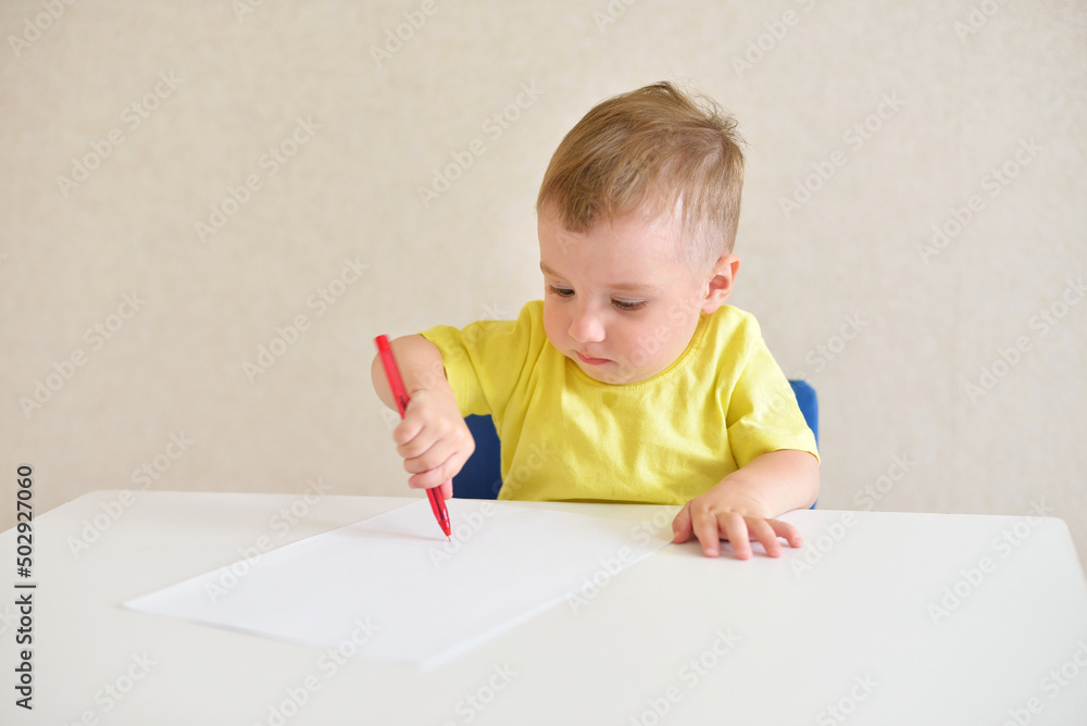 Foto de toddler boy plays draws on a piece of paper with a red pen ...