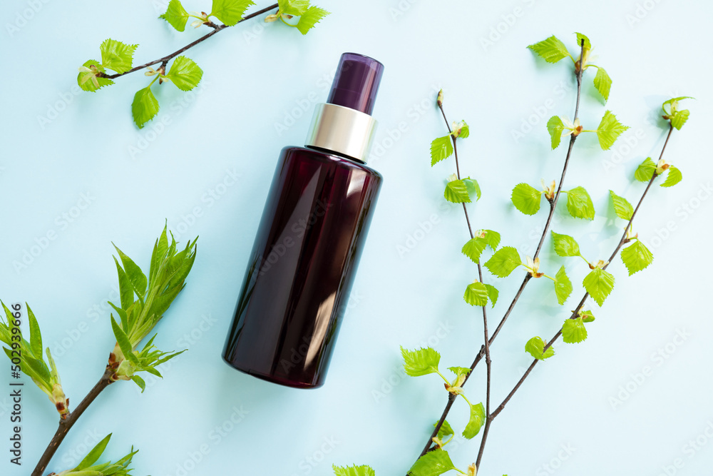 Brown cosmetic spray bottle and birch branches with young small leaves ...