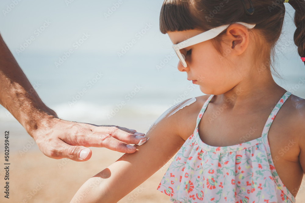 father smears her daughter with sunscreen on the beach in summer, the concept of safe tanning ...