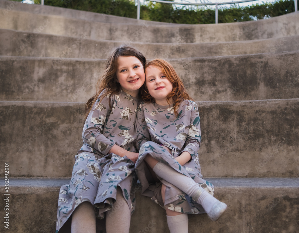 Portrait of two preteen sisters sitting in outdoor amphitheater smiling ...