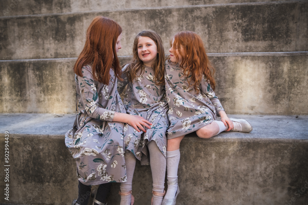 Three preteen sisters talking in outdoor amphitheater; girls wear ...