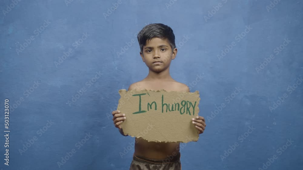 Sad Indian poor kid holding I am hungry sign board by looking at camera ...