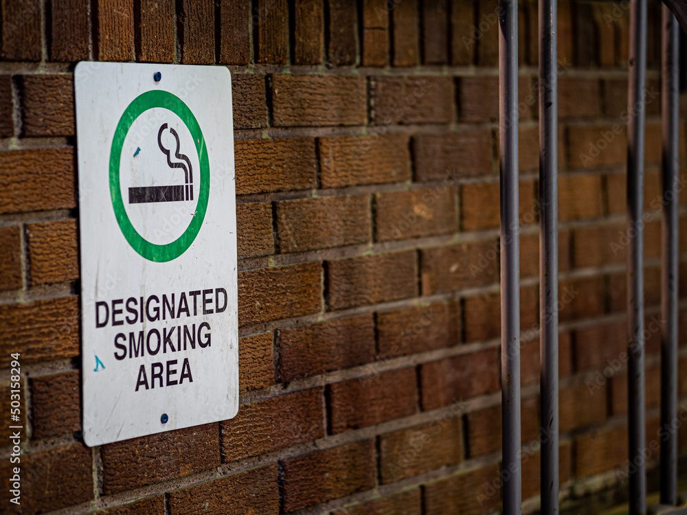 Sign of "Designated Smoking Area" pasted against a brown brick wall ...