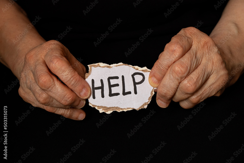 Old female hands hold a piece of paper with help text in the dark, help ...