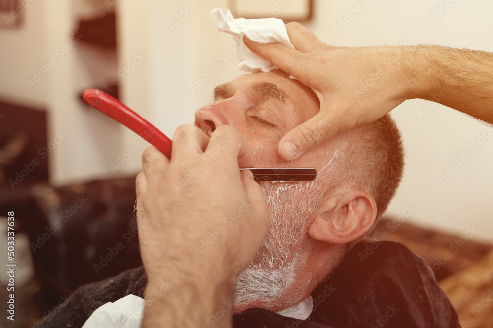 Shaving with a straight razor in a barbershop. A bearded old man being ...