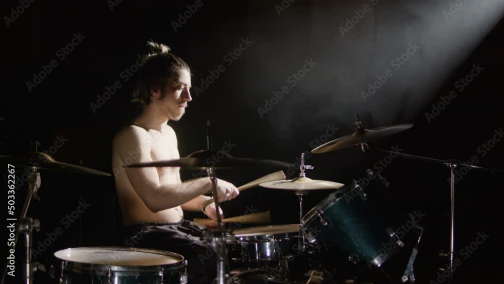 Energetic shirtless male drummer with beard playing drums at music ...