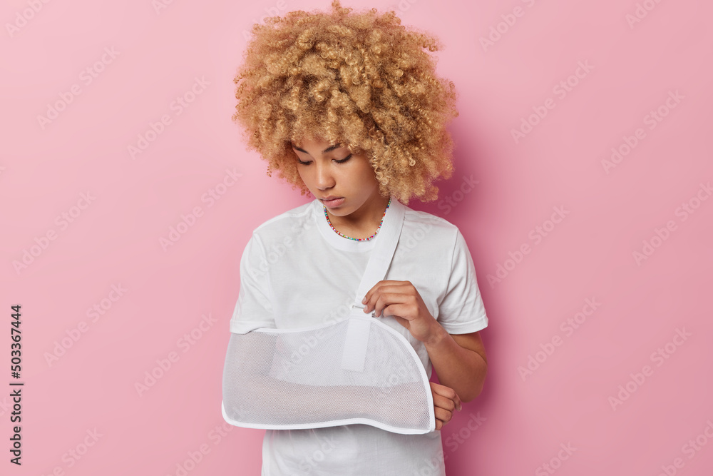 Serious curly haired woman with broken arm in splint suffers from hand ...