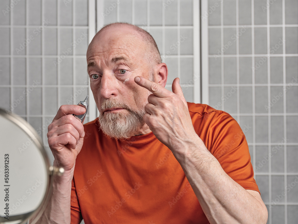 senior man is applying a retinol cream under his eyes, skincare and ...