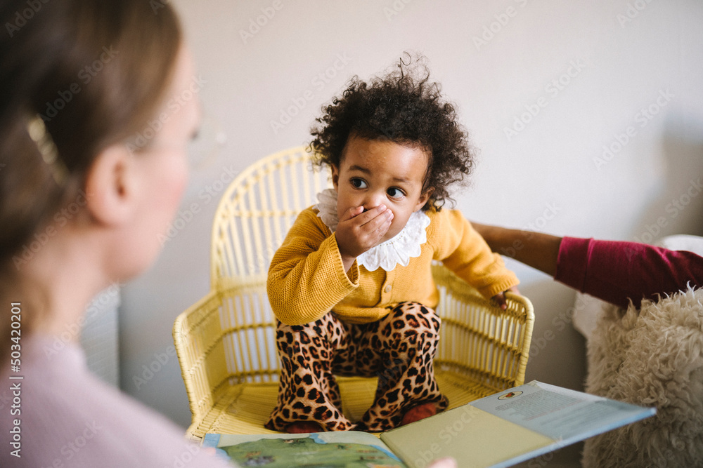 Girl crouching on chair and covering mouth Stock Photo | Adobe Stock