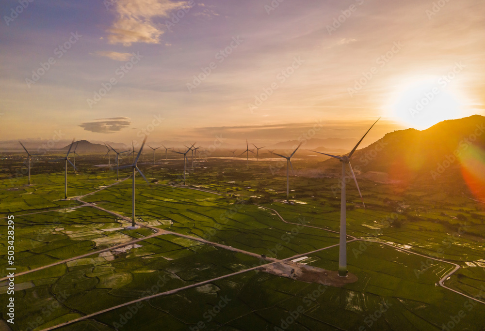 Wind turbines farm in a big green field at beautiful sunset generating ...