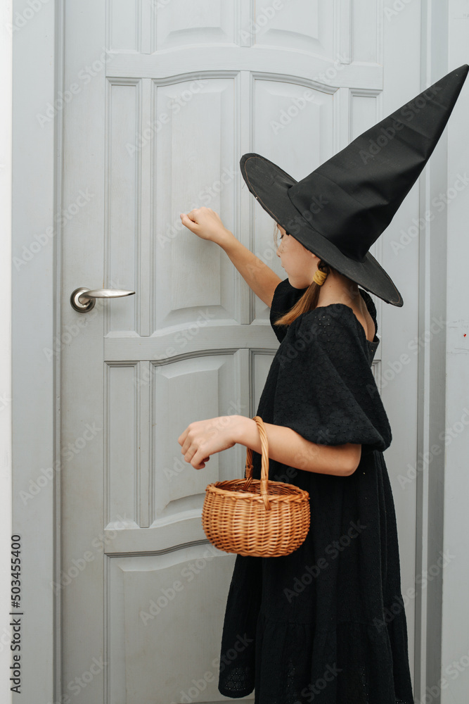 Little girl in a witch costume knocking on the door, trick or treating ...