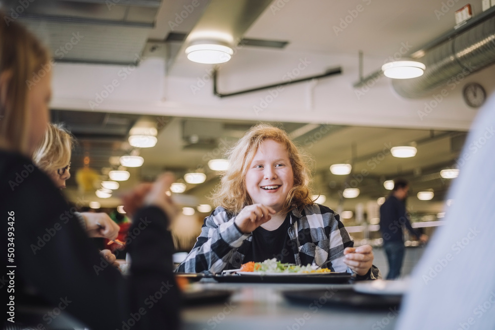 Smiling boy taking with friends during lunch break in cafeteria at ...