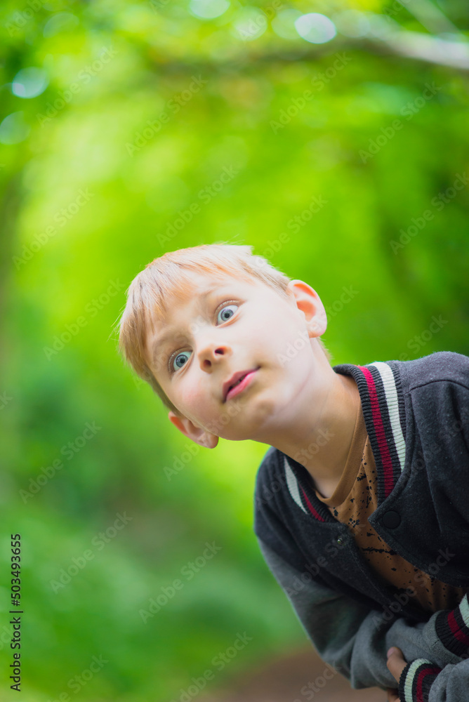 a boy of eight years old cheerfully looks into the frame on a green background of the forest ...
