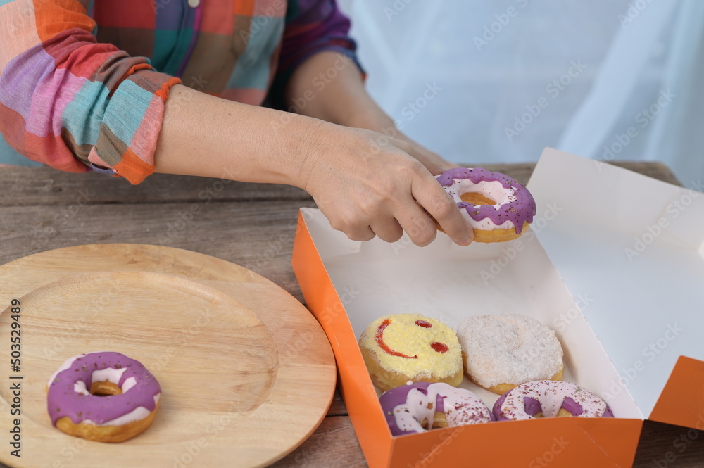 The woman's right hand was taking out a 1 purple glazed donut from an ...