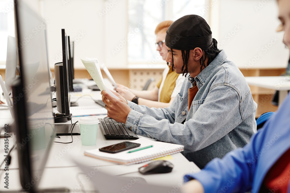 Side view portrait of black young man using computer in college library ...