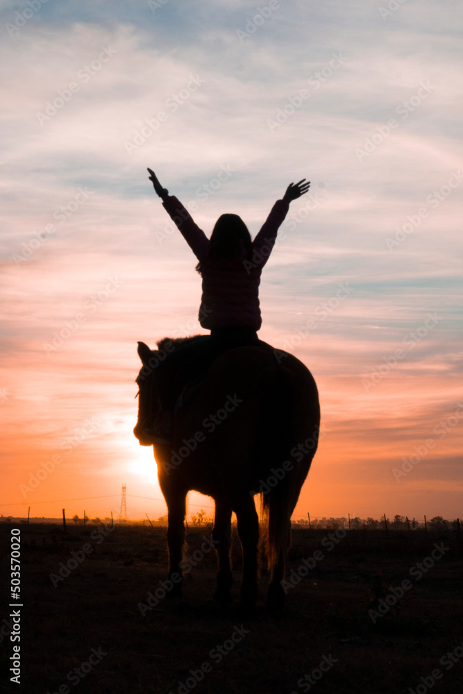 silueta de nena montada a caballo mirando el atardecer y levantando los ...