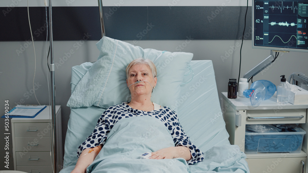 Elder patient with IV drip bag and nasal oxygen tube laying in bed ...
