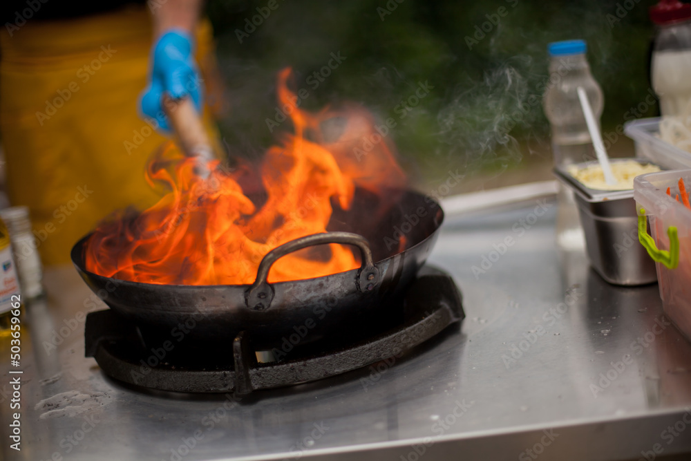 fire in the pan. Professional chef in a commercial kitchen cooking ...
