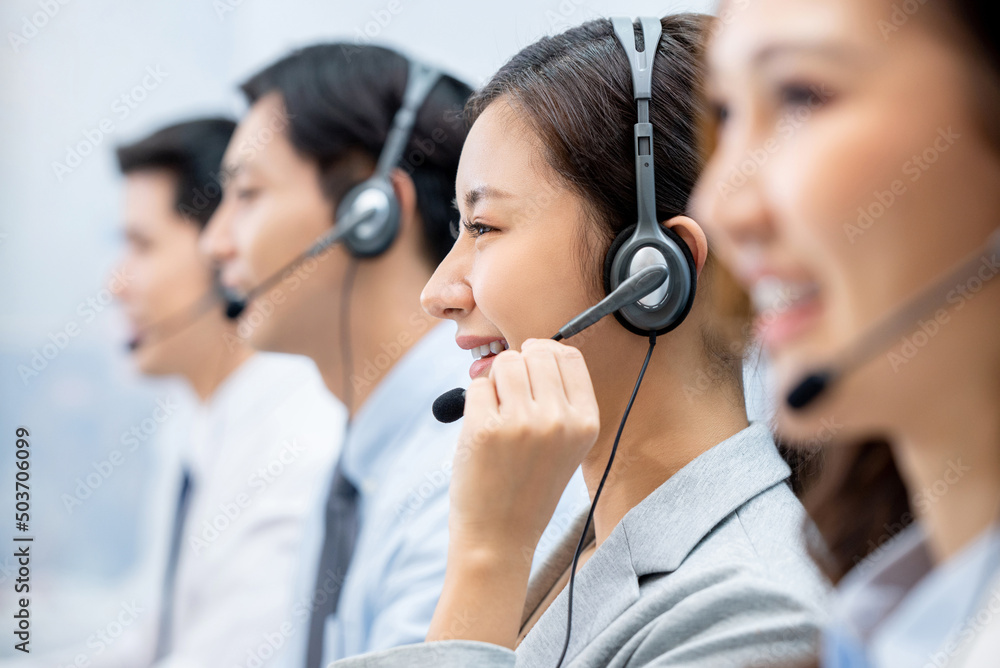 Side view of positive Asian woman telemarketer wearing headset with ...