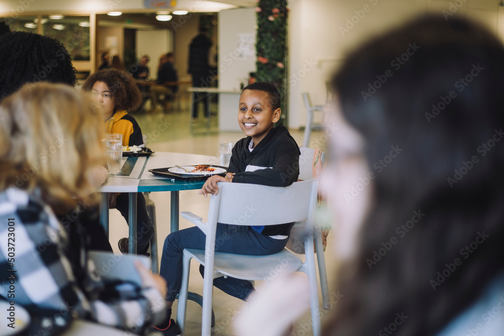 Side view of boy sitting on chair during lunch break in cafeteria at ...