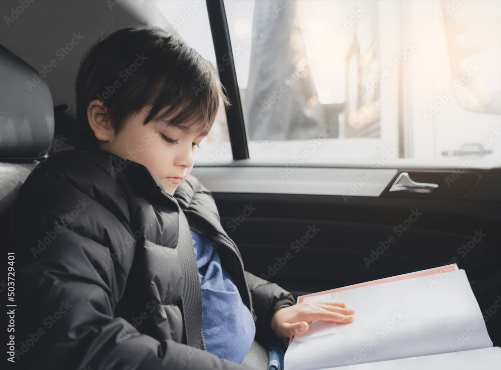 Kid siting on car seat and reading a book, Young boy sitting in safety ...