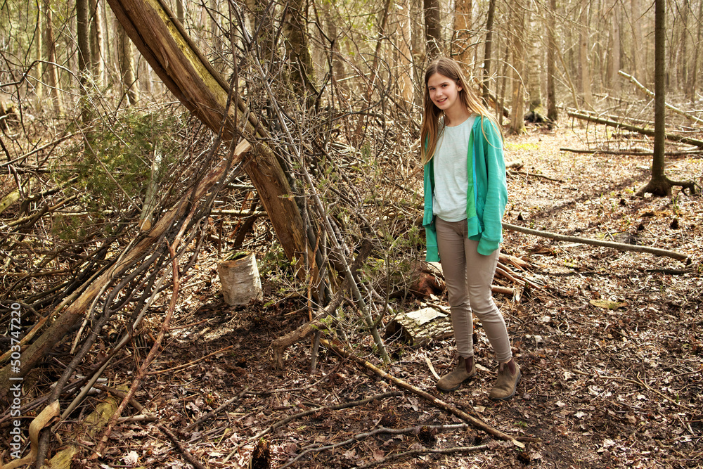 Young adolescent girl outside in the forest with lean-to tree fort ...