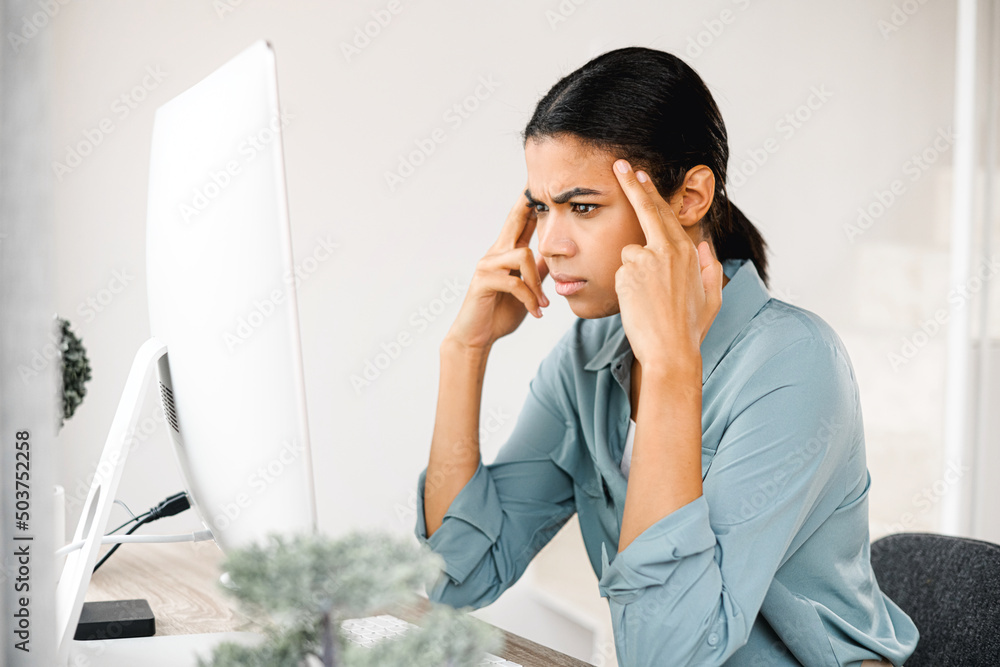 Tired multiracial young woman sitting at the table with computer and ...
