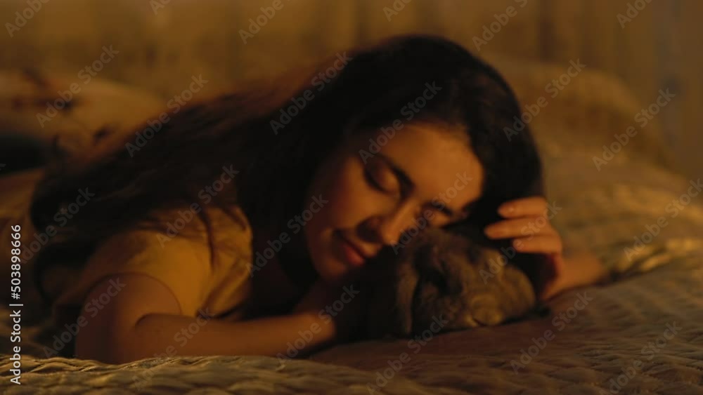 Portrait of a cute sleepy woman lying on a bed and stroking a lop-eared ...