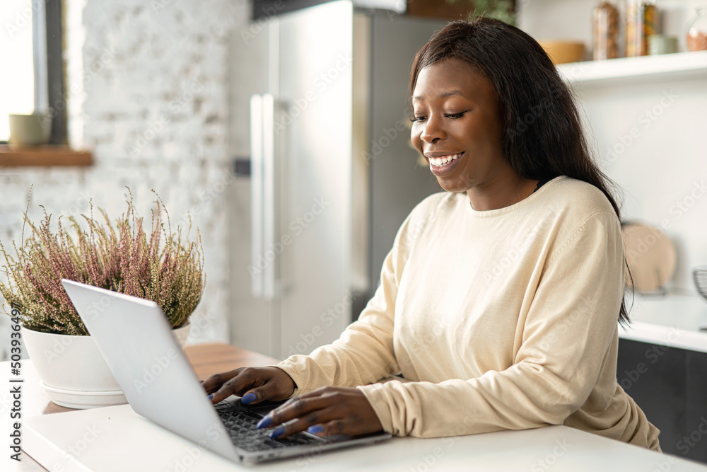 Smiling young woman sits on the countertop with laptop, spends time in ...