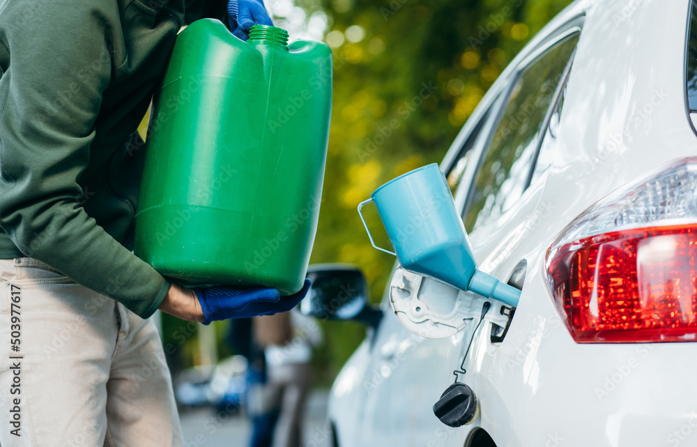 Young man pouring gasoline into an empty fuel tank from a plastic green ...