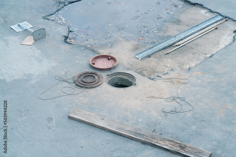 An open round hatch in the ground and metal hatch covers lying with ...