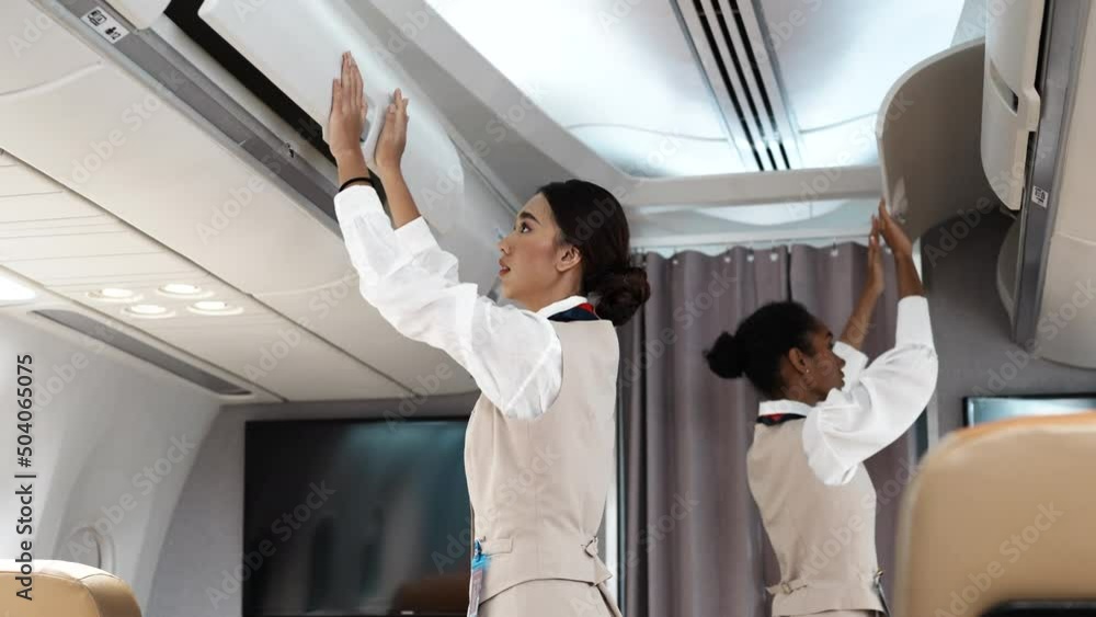 Two beautiful female flight attendants closing overhead cabinet luggage ...