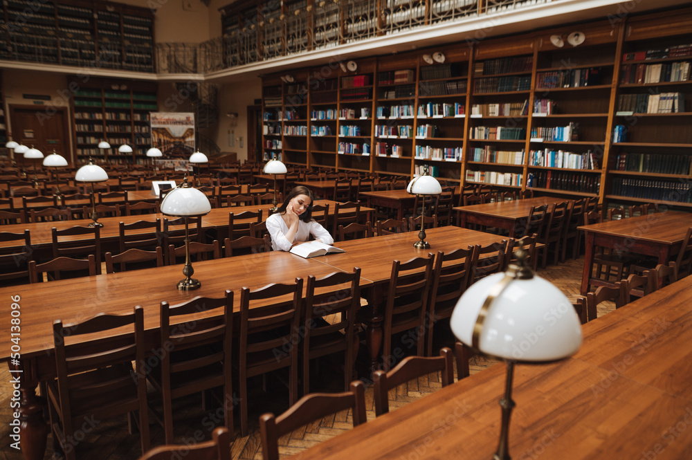 Female student sitting alone in a public old library and reading a book ...