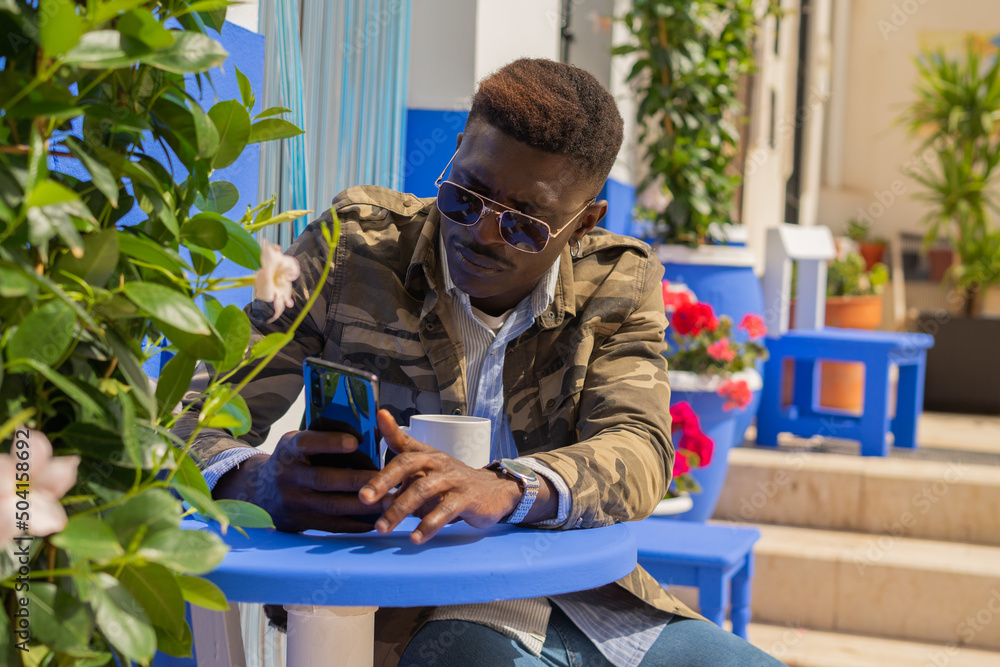 Chico sentado en la terraza de una casa, entre flores, con una taza de ...