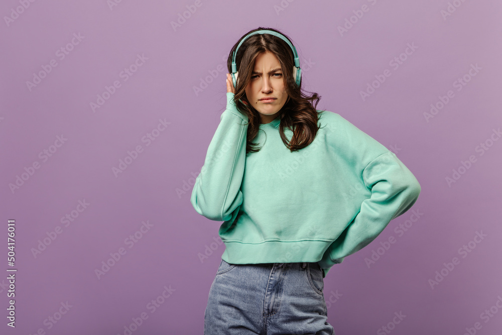 Young caucasian girl frowningly looks at camera listening to music ...