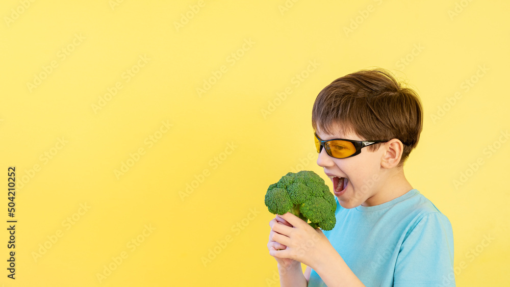 The boy is holding broccoli. Portrait of a funny boy in a blue t-shirt ...